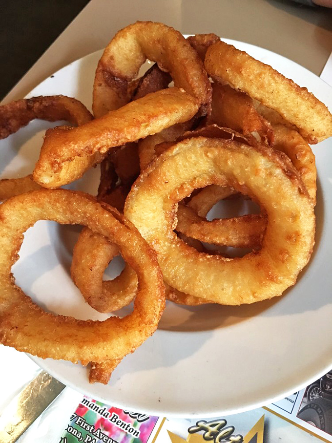 Onion rings with architectural integrity &ndash; crispy, golden halos that shatter satisfyingly with each bite while maintaining their perfect circular form.