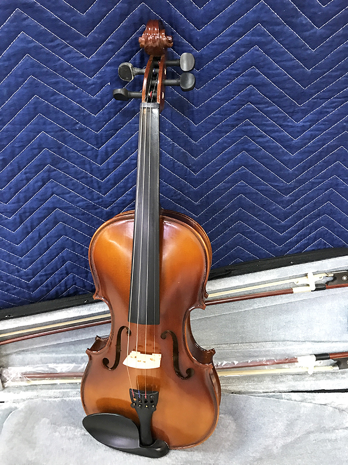 A violin awaits its next musician against a quilted blue backdrop. Someone's abandoned hobby could become your child's passion&mdash;musical instruments often get their second wind here.