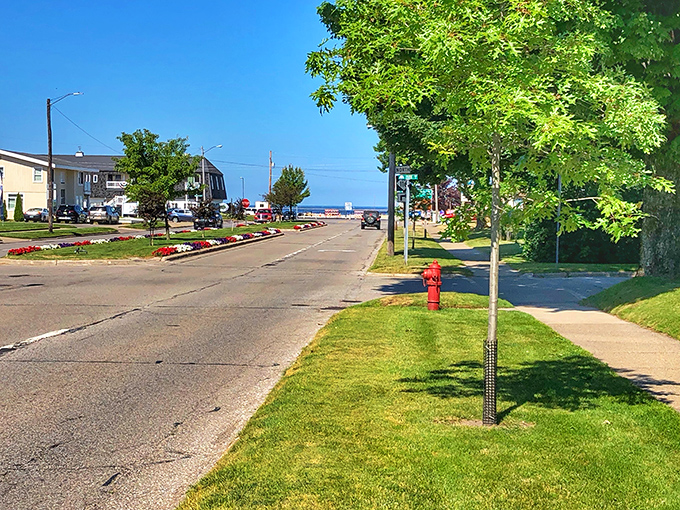 A sunny summer day in downtown Ludington, with manicured lawns, tree-lined sidewalks, and a glimpse of Lake Michigan in the distance.