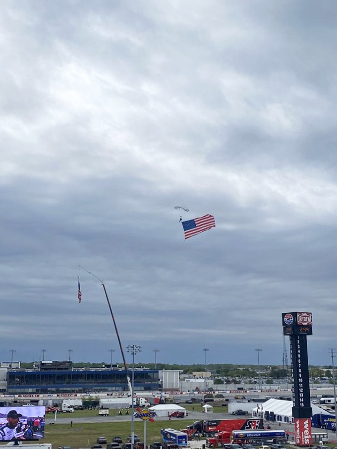 A patriotic parachutist delivers Old Glory to the speedway grounds, adding a touch of aerial drama to race day festivities.