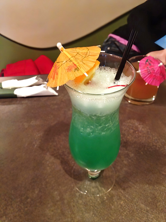 Vacation in a glass! This vibrant blue-green cocktail topped with playful paper umbrellas brings tropical vibes to the Midwest &ndash; no passport required.