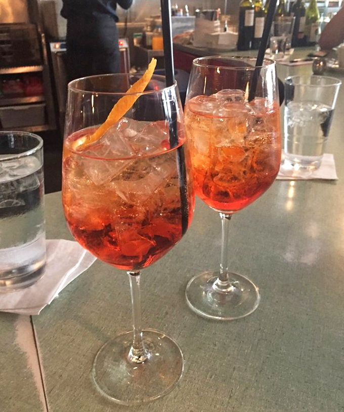 Two Aperol Spritzes stand like sunset-colored sentinels, ready to wash away workday worries with each bubbly sip.