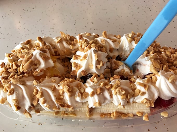 Banana split architecture at its finest&mdash;whipped cream mountains, crunchy nut valleys, and that blue spoon standing ready for your excavation expedition.
