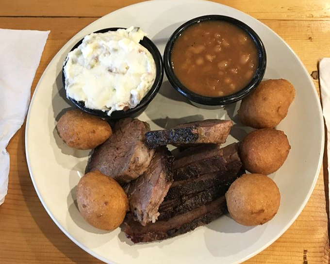A trio of smoked excellence: ribs, beans, and cornbread, with hushpuppies standing guard around the plate like delicious little sentinels.