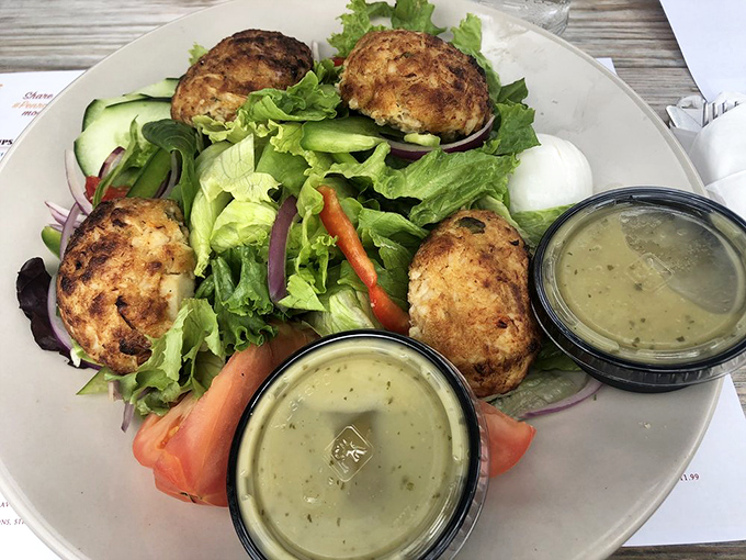 Garden-fresh salad serving as the red carpet for those golden-brown crab cakes. The dressing cups wait patiently for their supporting role.