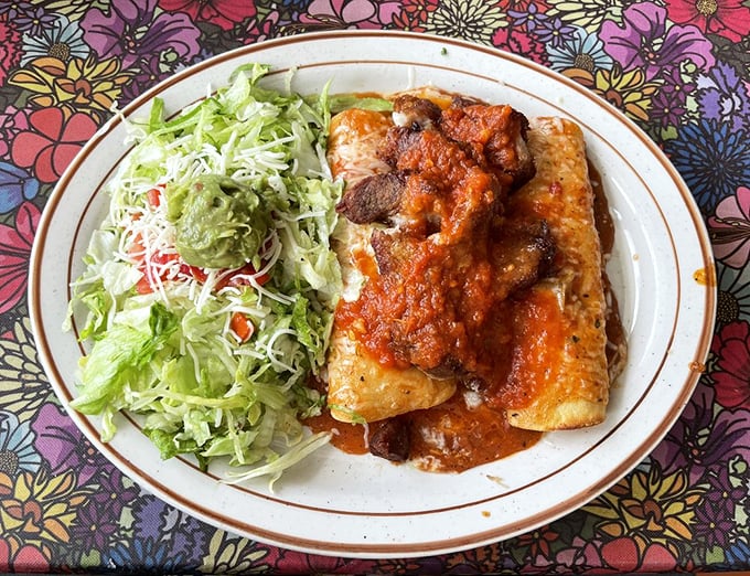 The Enchiladas Rancheras arrive draped in a red sauce so rich it deserves its own tax bracket. The side salad is just pretending you care about balance.