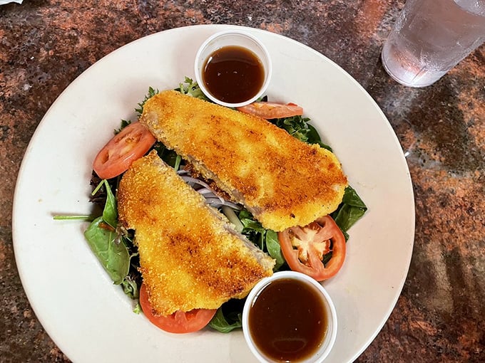 This isn't just fried fish&mdash;it's a golden-crusted masterpiece resting on fresh greens with tomatoes, a reminder that simple food done right is culinary poetry.