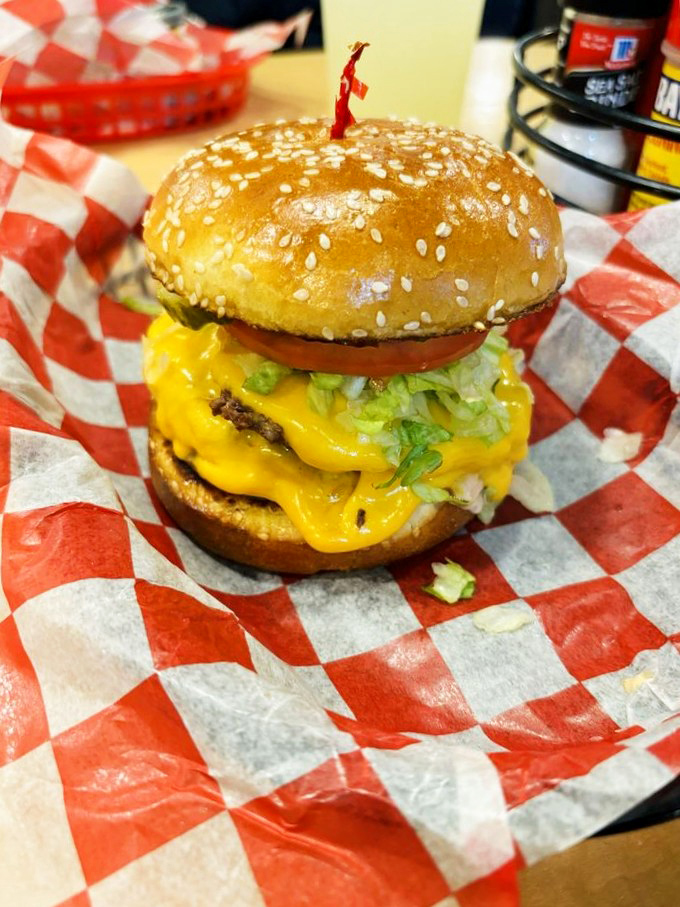 Cheese cascading like a yellow waterfall over fresh lettuce and tomato. This towering creation demands both hands and your complete attention&mdash;conversation can wait.