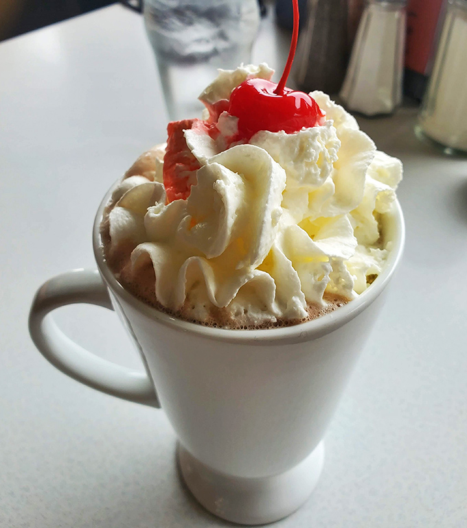 Hot chocolate elevated to an art form&mdash;whipped cream mountain, cherry on top, and somewhere beneath it all, liquid happiness waiting to be sipped.