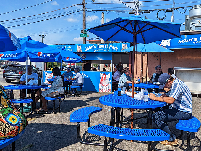 The outdoor dining area provides the authentic Philly experience: industrial views, blue tables, and the communal joy of public sandwich worship.
