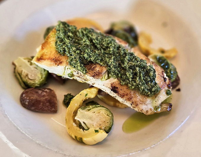 The halibut arrives wearing its finest herb pesto coat, lounging comfortably on a bed of seasonal vegetables like it owns the place.