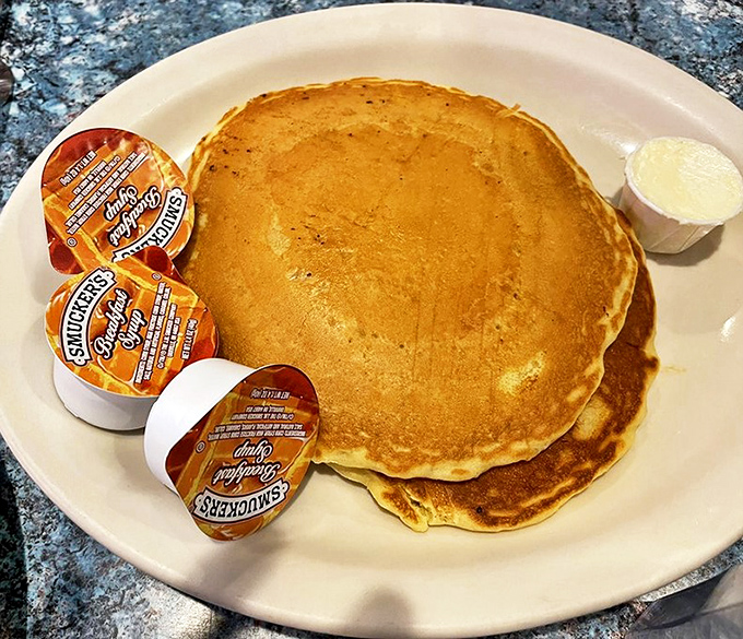 Pancakes so perfectly golden they belong in Fort Knox, served with those little cups of syrup that somehow never quite seem enough for the magnificent stack.