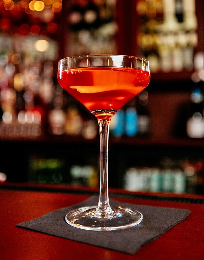 A cocktail the color of a Wisconsin sunset, served in a glass so elegant it makes you sit up straighter just holding it.