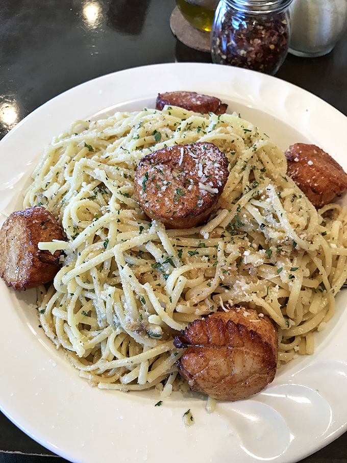Perfectly seared scallops perch atop a nest of pasta like culinary royalty surveying their delicious domain.