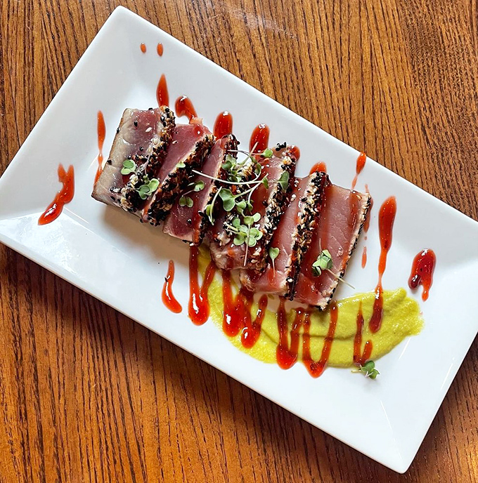 Sesame-crusted tuna, seared rare and sliced like jewels, resting on a vibrant sauce—proof that sometimes the most beautiful dishes are the simplest.