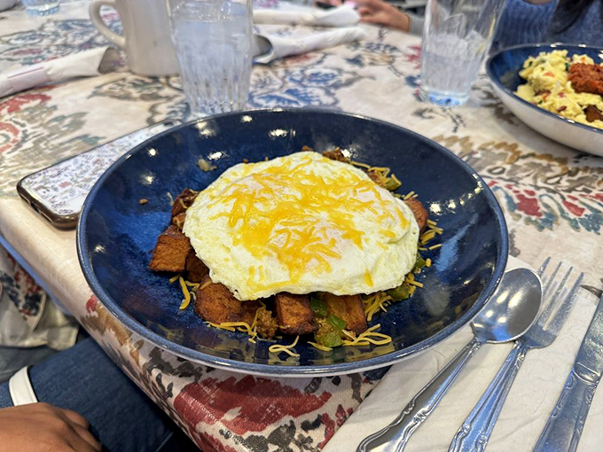 A blue bowl cradling breakfast treasures topped with melted cheese. Morning comfort food that hugs you from the inside.