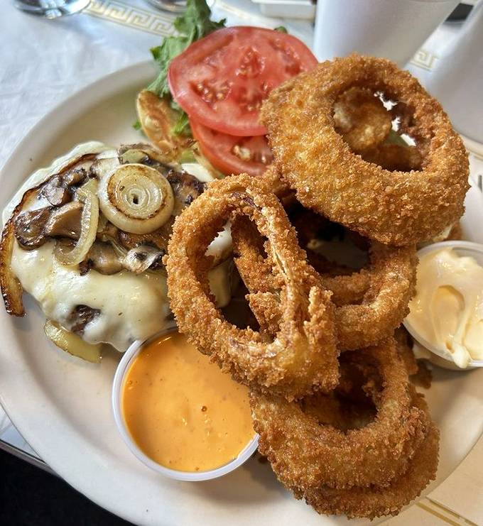Onion rings stacked like golden halos around a burger that's been kissed by the flat-top gods. The side of cheese sauce isn't optional&mdash;it's essential. 