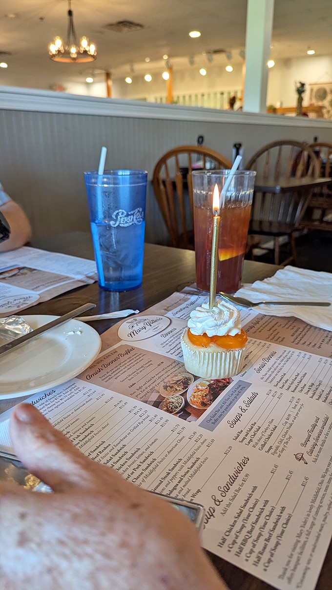 A birthday cupcake with a candle waits patiently while drinks stand guard. Some celebrations require proper hydration before the sugar rush.