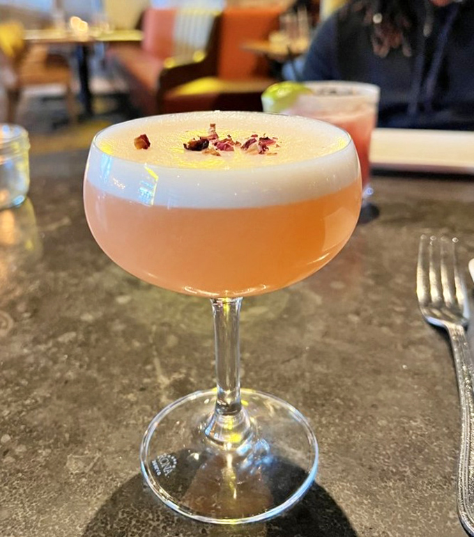 A cocktail that looks like liquid sunshine, garnished with flower petals because drinking should be as beautiful as it is delicious. 