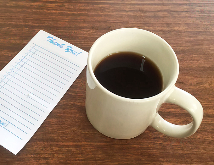 Simple white mug, black coffee, checkered receipt pad&mdash;the holy trinity of diner breakfast. No fancy latte art needed when the coffee itself tells the story.