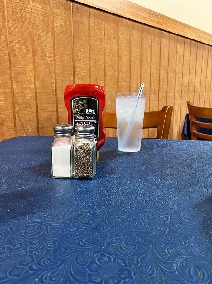 The holy trinity of Texas dining: salt, pepper, and fancy ketchup, standing at attention on blue tablecloths that have witnessed countless food epiphanies.