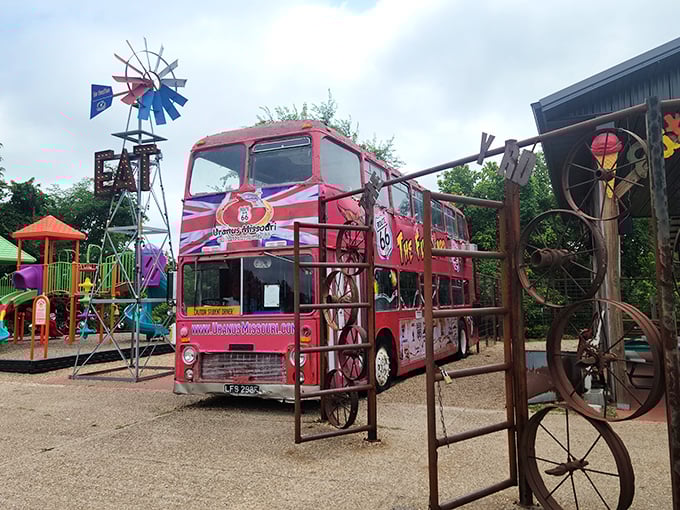 A classic British double-decker bus painted in vibrant colors stands among vintage farm equipment, creating a delightful anachronism that somehow makes perfect sense here.