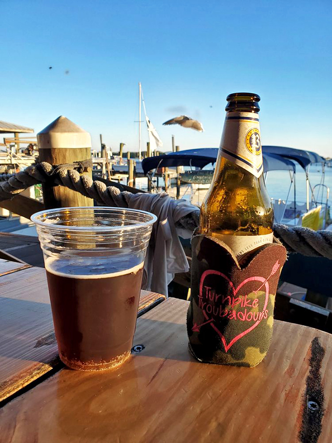 A cold beer and a plastic cup of dark brew sit on a dockside table, soaking in the golden hour glow with boats, gulls, and calm Florida waters in the background.