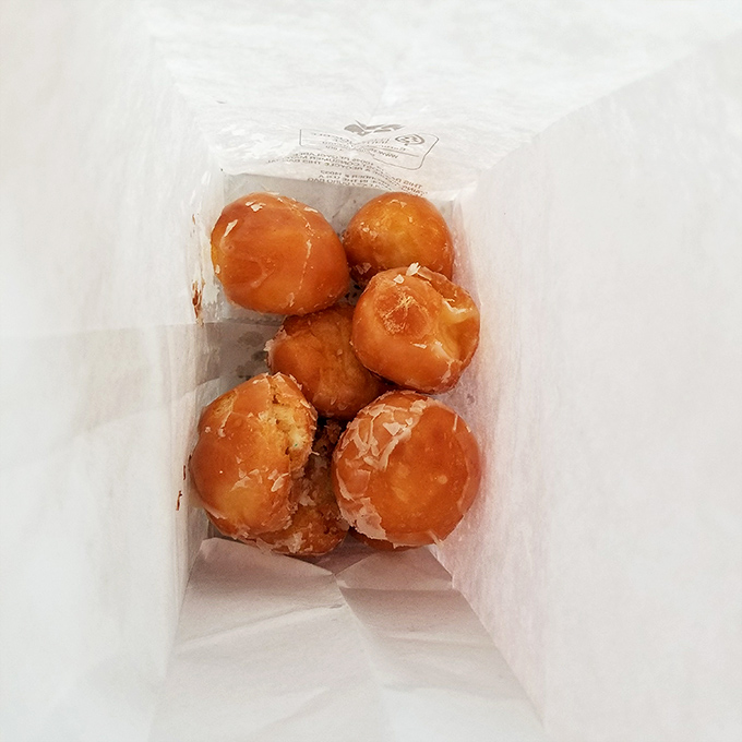 The white paper bag&mdash;a humble vessel for pure joy. Six glazed donut holes nestled together like edible pearls of happiness.