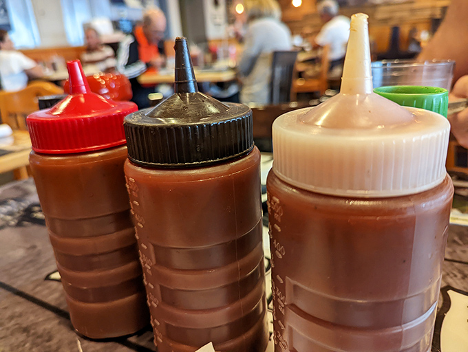 Sauce bottles lined up like flavor soldiers, each one ready to deploy a different dimension to your barbecue experience&mdash;choose your adventure wisely.
