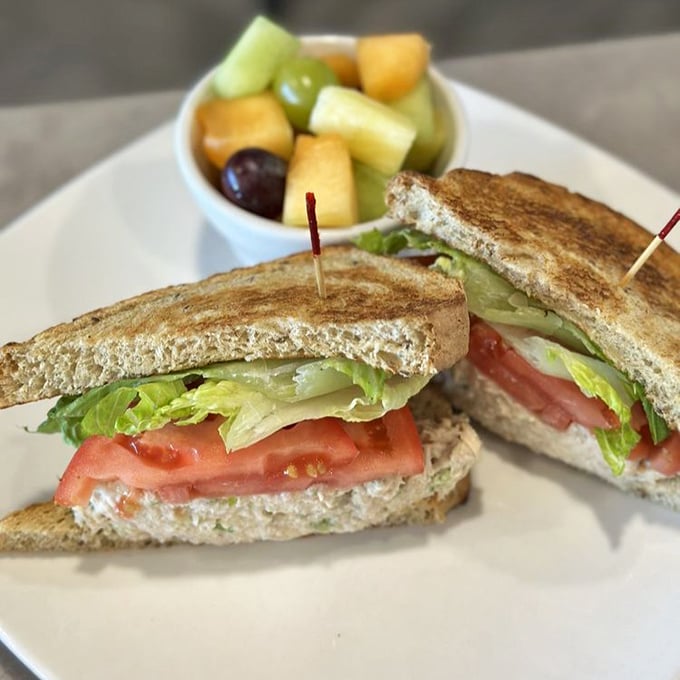 A sandwich that understands balance: crisp lettuce, juicy tomatoes, and fresh bread with a side of fruit that makes healthy choices delicious.