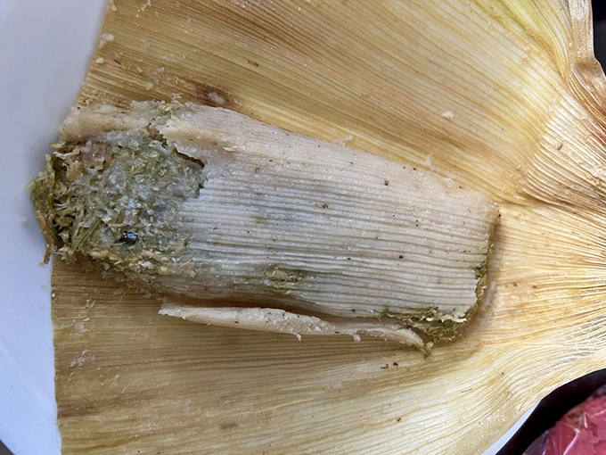 The chicken and green sauce tamale reveals its secrets&mdash;tender meat embraced by vibrant salsa verde, all wrapped in nature's perfect to-go container. Portable perfection at its finest.