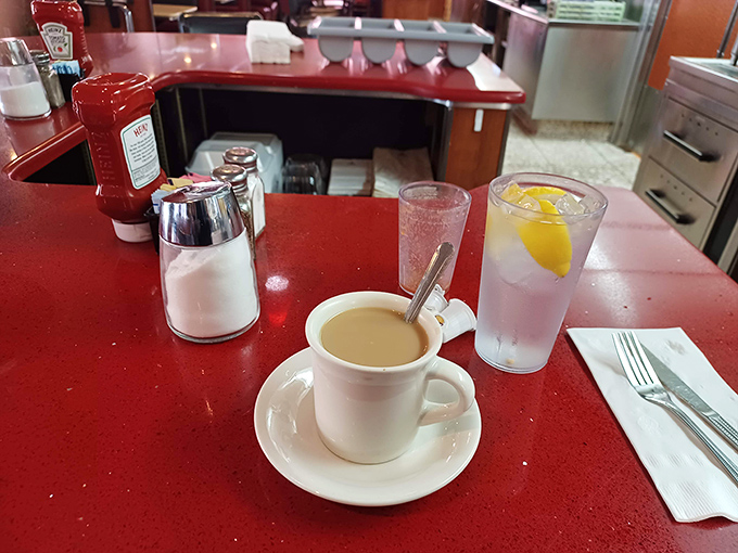 Coffee in a classic white mug on a cherry-red counter&mdash;the morning ritual that makes everything possible. Diners understand this sacred truth.