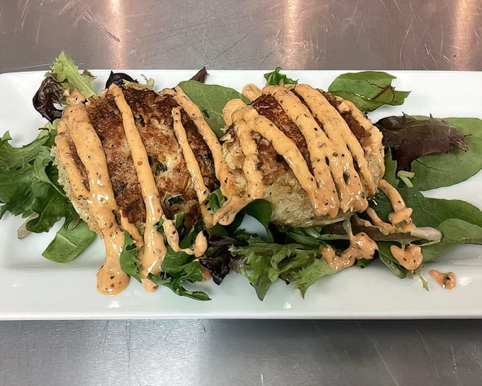 Crab cakes perched on fresh greens with drizzles of sauce. Ocean treasures transformed into crispy-creamy Southern delights