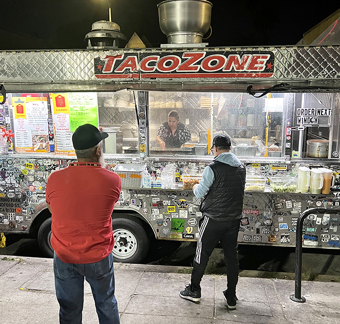 The sacred ritual of late-night taco procurement: customers patiently awaiting their turn at the window, united by hunger and excellent life choices.