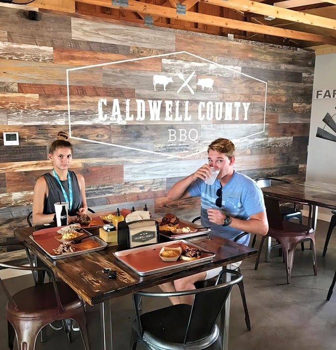 The universal language of barbecue brings people together at wooden tables beneath that signature rustic wall that's Instagram-famous for good reason.