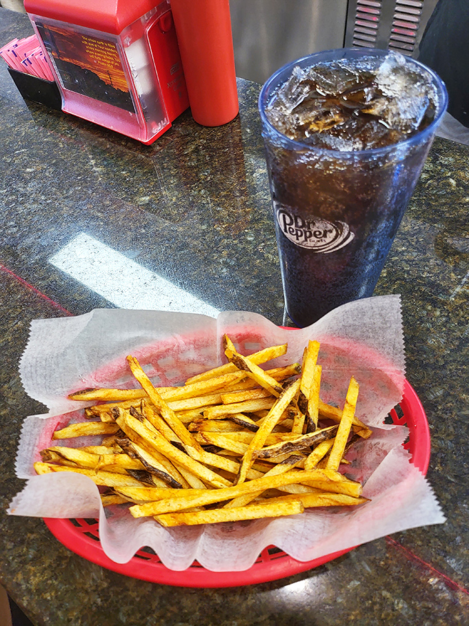 Hand-cut fries that actually taste like potatoes, served with zero pretension in a red basket. The Dr Pepper provides necessary lubrication.