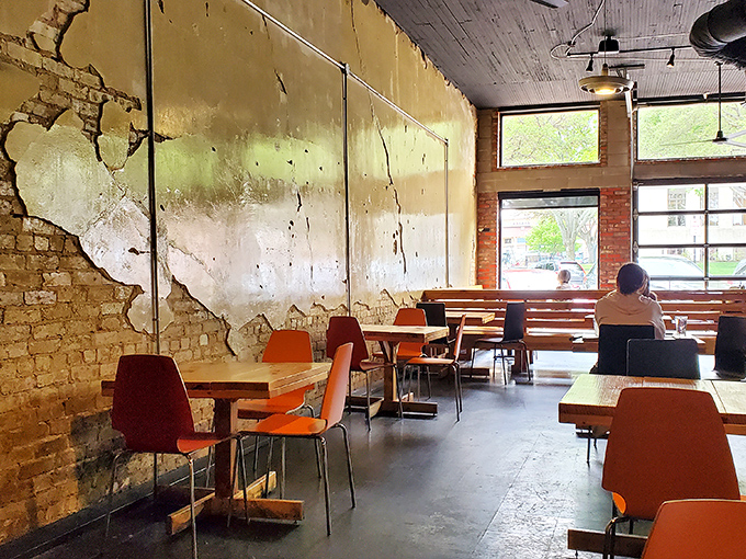 The distressed walls tell stories while orange chairs add pops of color, creating a space where lingering over that second cup of coffee feels not just allowed but encouraged.