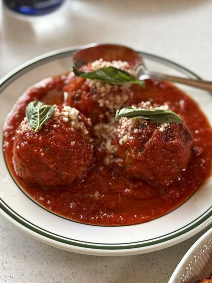 Meatballs swimming in sauce so rich it probably has its own accountant. The basil garnish is just showing off.