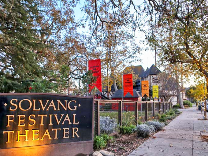 The Solvang Festival Theater brings culture under the stars, with colorful banners announcing performances against a backdrop of Danish-inspired architecture.