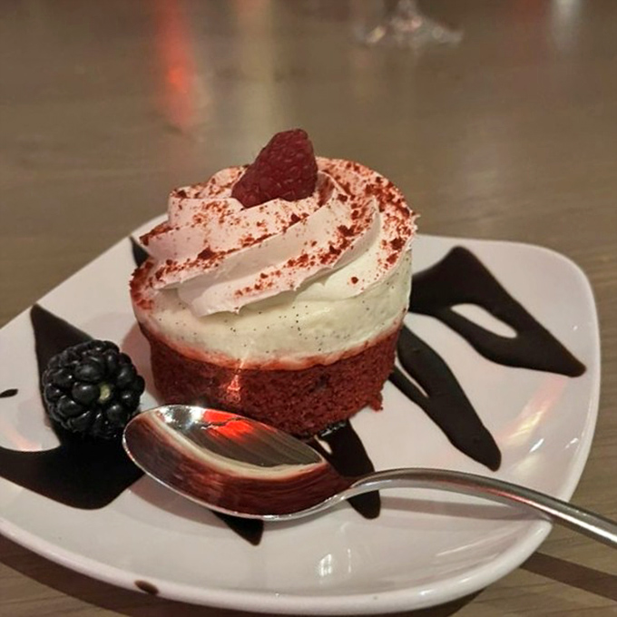 Red velvet cupcake topped with a cloud of cream cheese frosting and a single raspberry&mdash;because sometimes dessert should wear a tiny hat.