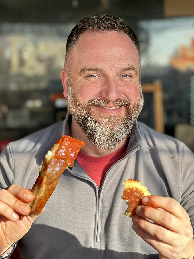 The image shows a smiling patron enjoying what appears to be barbecue delights—the universal expression of someone who's found their happy place.