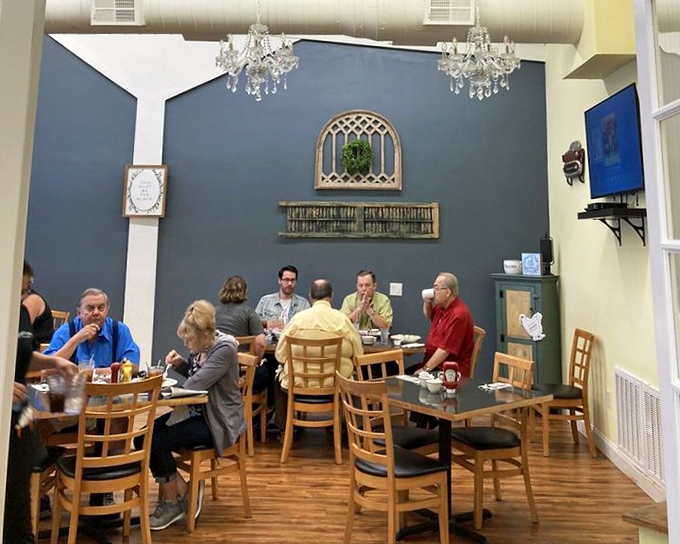 The blue accent wall and crystal chandeliers create an unexpected touch of elegance. Diners deep in conversation prove good food brings people together.