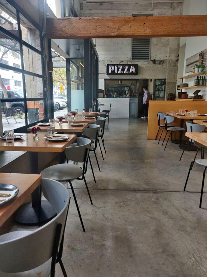 Simple wooden tables, concrete floors, and that glorious "PIZZA" sign—like a minimalist poem to carbohydrates that speaks directly to the soul.