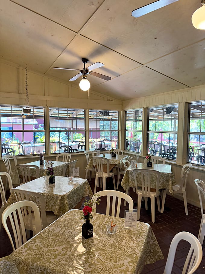 Sunlight streams through windows in this airy dining space, where lace tablecloths and simple flowers create an atmosphere of unpretentious elegance.