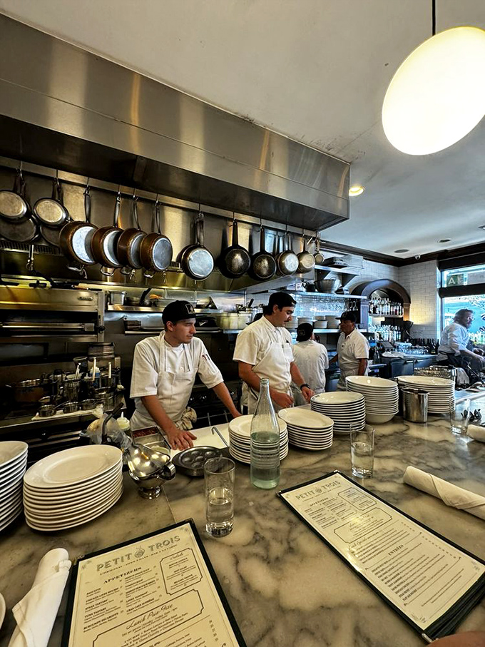 The kitchen at Petit Trois operates with balletic precision. White-coated chefs arrange plates on marble counters while copper pots hang overhead like culinary medals of honor.
