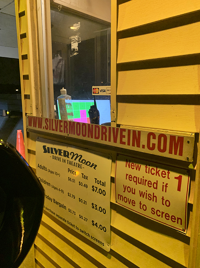 The ticket window glows with possibility, a portal to another world where movies cost less than your morning latte.