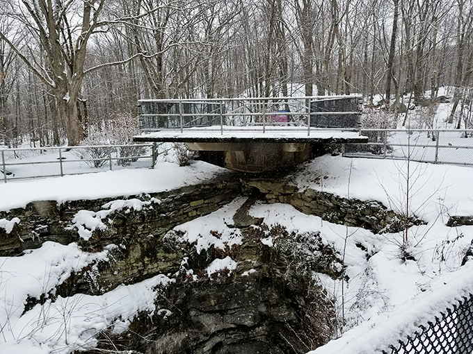 Winter transforms the pothole into a snow-rimmed geological wonder. The stark white landscape highlights the dramatic depth of this natural formation.