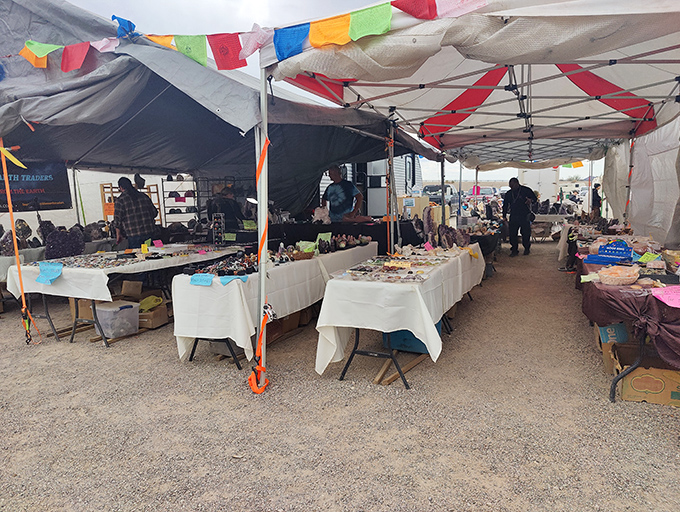 Colorful prayer flags flutter above white-clothed tables laden with treasures, creating a bazaar atmosphere where desert winds carry whispers of bargains.