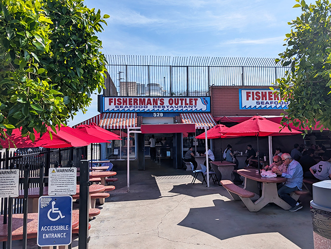 The unassuming exterior of Fisherman's Outlet, where those vibrant red umbrellas promise something special is happening beneath them. No fancy facade needed when the seafood speaks for itself.