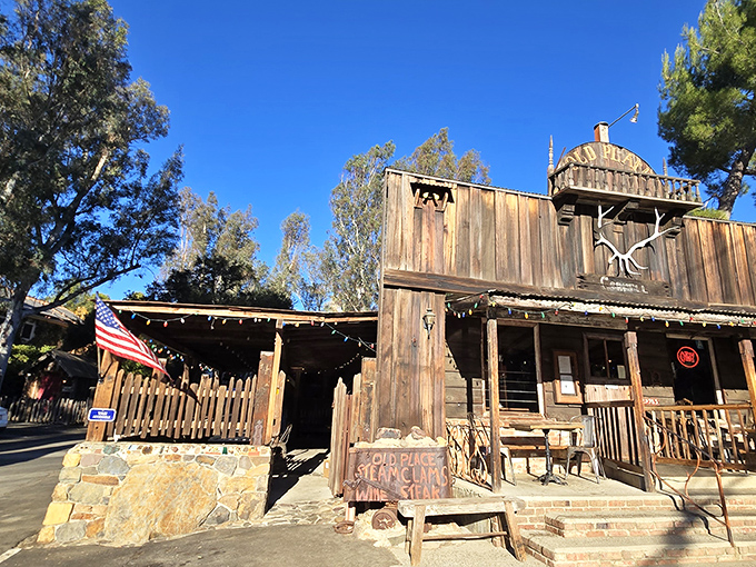 Like a movie set from a forgotten Western, The Old Place stands defiantly against time, its weathered wooden facade and American flag promising authentic frontier hospitality.